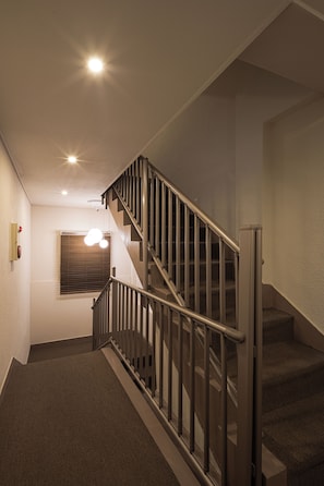 Uma escadaria com corrimão de metal, degraus com carpete e um aparelho de iluminação acima.