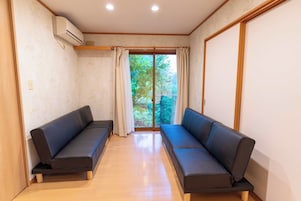 Um quarto com dois sofás pretos, piso de madeira, janela com cortinas e um aparelho de ar condicionado.