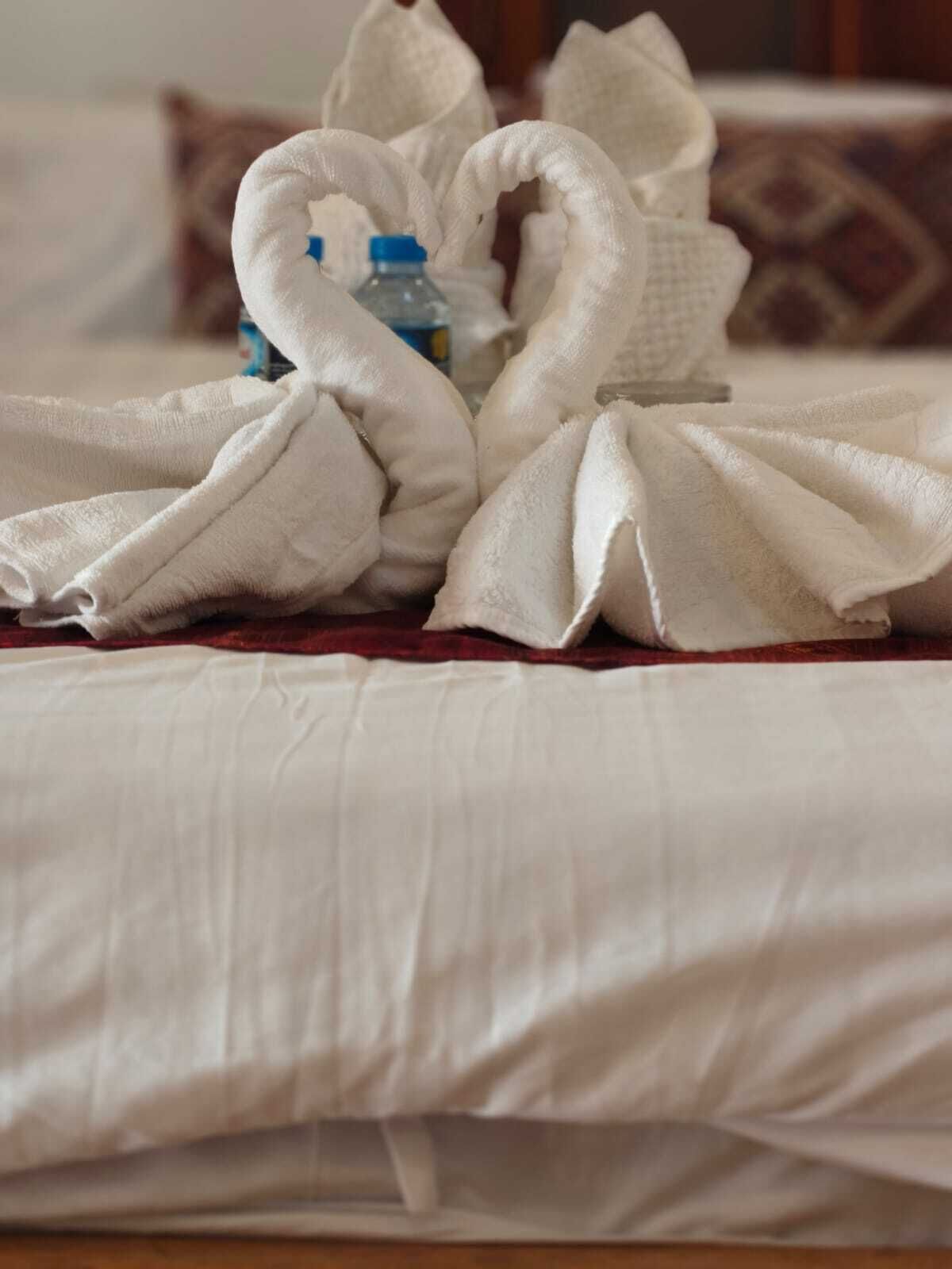 Cama com colcha branca e toalha dobrada em formato de cisne.