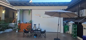Uma pousada com balcão de recepção, área de estar ao ar livre, um violão e um grande guarda-sol.
