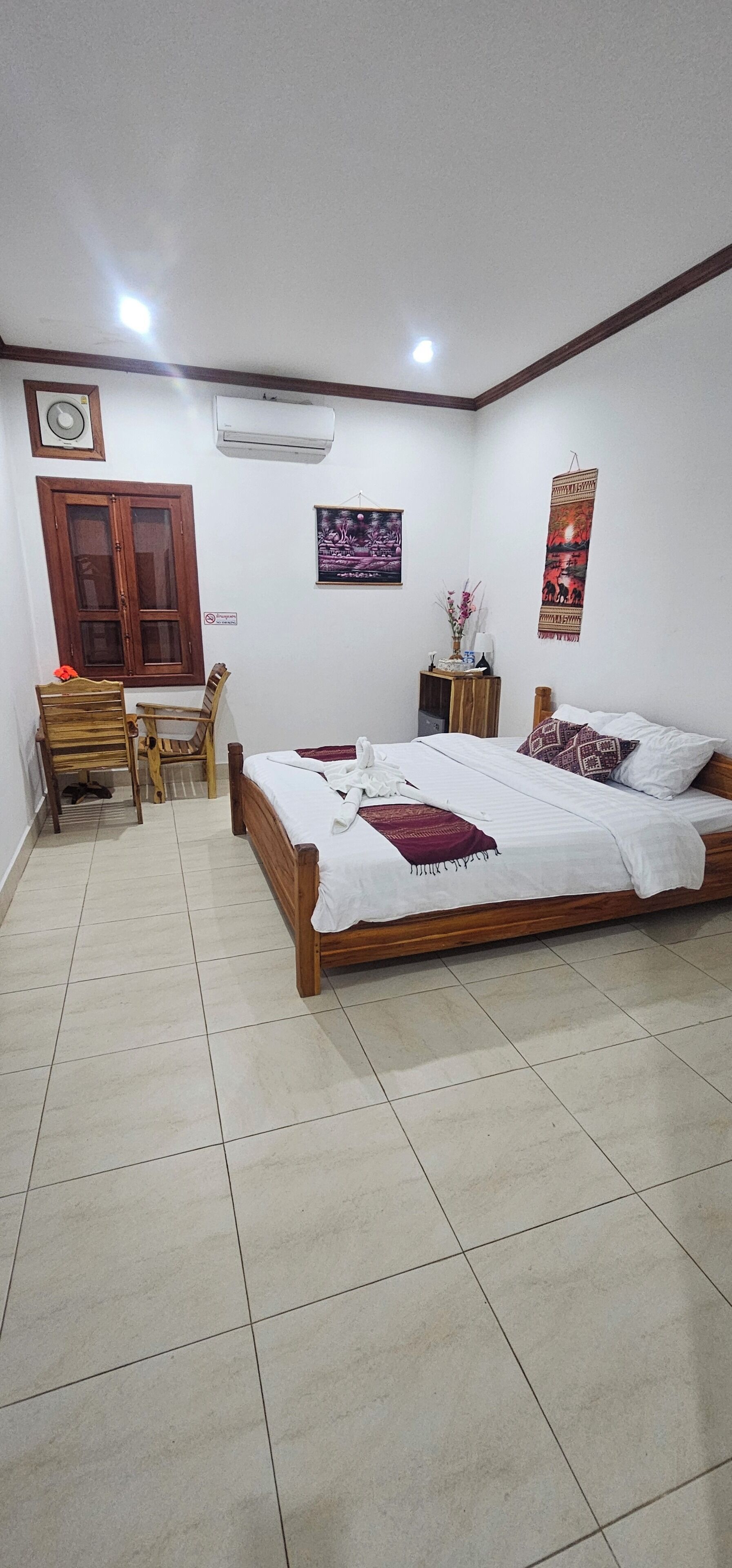 Quarto com cama, escrivaninha e cadeira. Há uma janela com moldura de madeira e um ar condicionado fixado na parede.