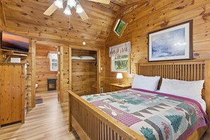 Quarto de cabana de madeira com uma cama, uma TV, uma janela e um quadro na parede.