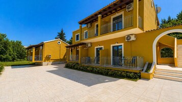 Um edifício amarelo com um pátio ladrilhado, varandas e uma escadaria que leva a uma entrada.