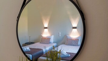 Espelho circular refletindo um quarto com duas camas, cada uma com travesseiro e cobertor.