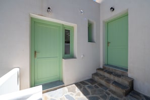 Um edifício com duas portas verdes, uma pequena janela e degraus de pedra que levam à entrada.