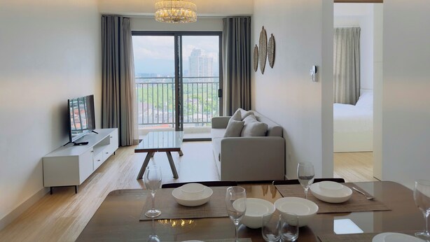 Uma sala de estar moderna com um sofá, mesa de jantar posta com pratos e copos, televisão e um candelabro.