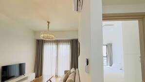 Uma sala de estar moderna com uma televisão de tela plana, uma mesa de centro de madeira, um sofá bege e um lustre.