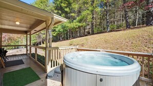 Uma banheira de hidromassagem em um deck de madeira com área coberta e vista para uma área arborizada.