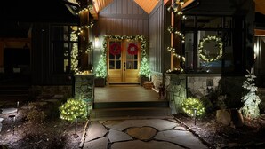 Entrada de uma casa de madeira com um caminho de pedra, decorada com luzes de Natal e guirlandas.