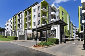 Um edifício residencial com vários andares, varandas, entrada fechada por portão e galeria coberta.