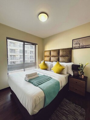Quarto de hotel com cama, mesa de cabeceira, persianas e luz no teto.