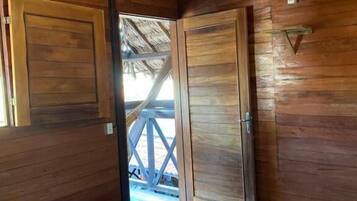 Quarto de madeira com uma cama, um candeeiro pendente e vista para um terraço ao ar livre.