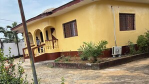 Um edifício amarelo com varanda, janela com grades e um pequeno jardim.