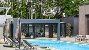 Uma área de piscina moderna com espreguiçadeiras, um espaço de estar coberto e vista para as árvores ao redor.