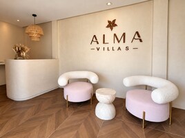 Uma área de recepção com design moderno, destacando um balcão e duas cadeiras de formas originais com pufes redondos.
