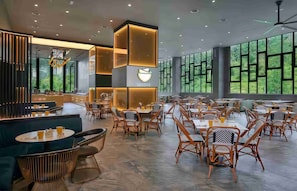 Interior de restaurante moderno com um letreiro Loxors central, grandes janelas e uma mistura de mesas redondas e quadradas com cadeiras de vime.