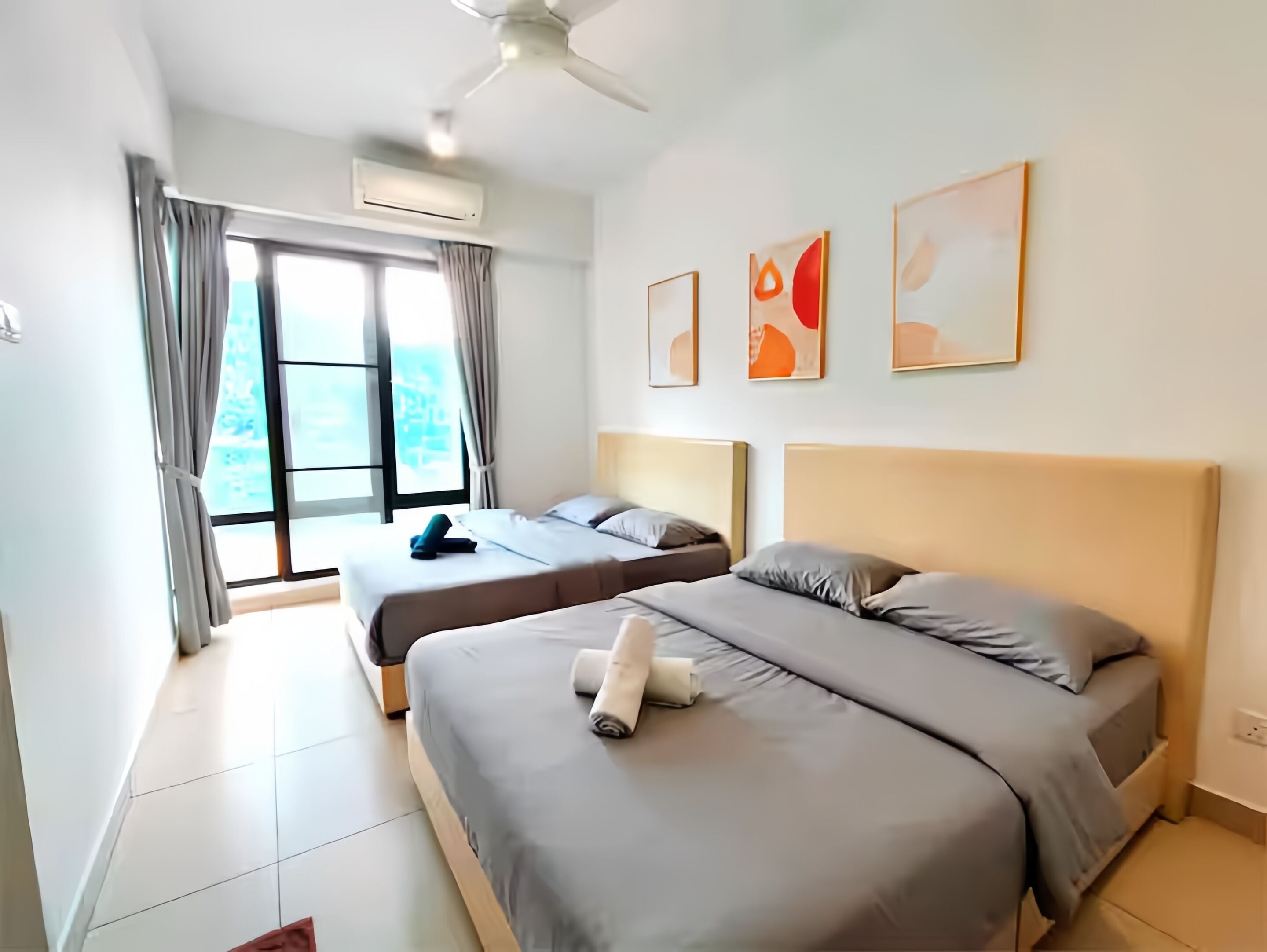 Quarto de hotel com duas camas, um ventilador de teto, aparelho de ar condicionado e uma janela grande com cortinas.