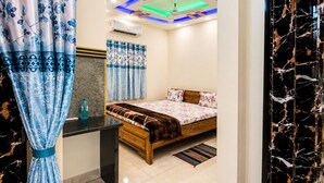 Quarto com cama, cortinas, ar condicionado, luminária no teto e mesa de cabeceira de madeira.