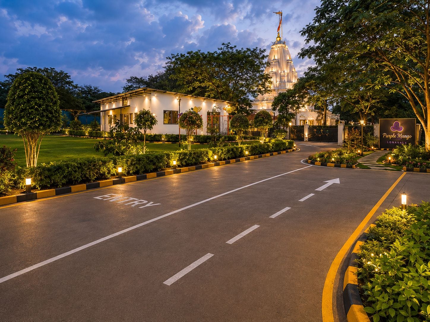 Entrada de um hotel com uma alameda bem iluminada, uma placa de identificação e um edifício grande com uma cúpula ao fundo.