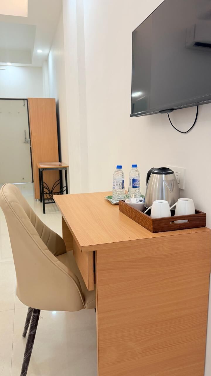 Quarto de hotel com escrivaninha de madeira, uma cadeira, televisão fixada na parede e máquina de café sobre a escrivaninha.