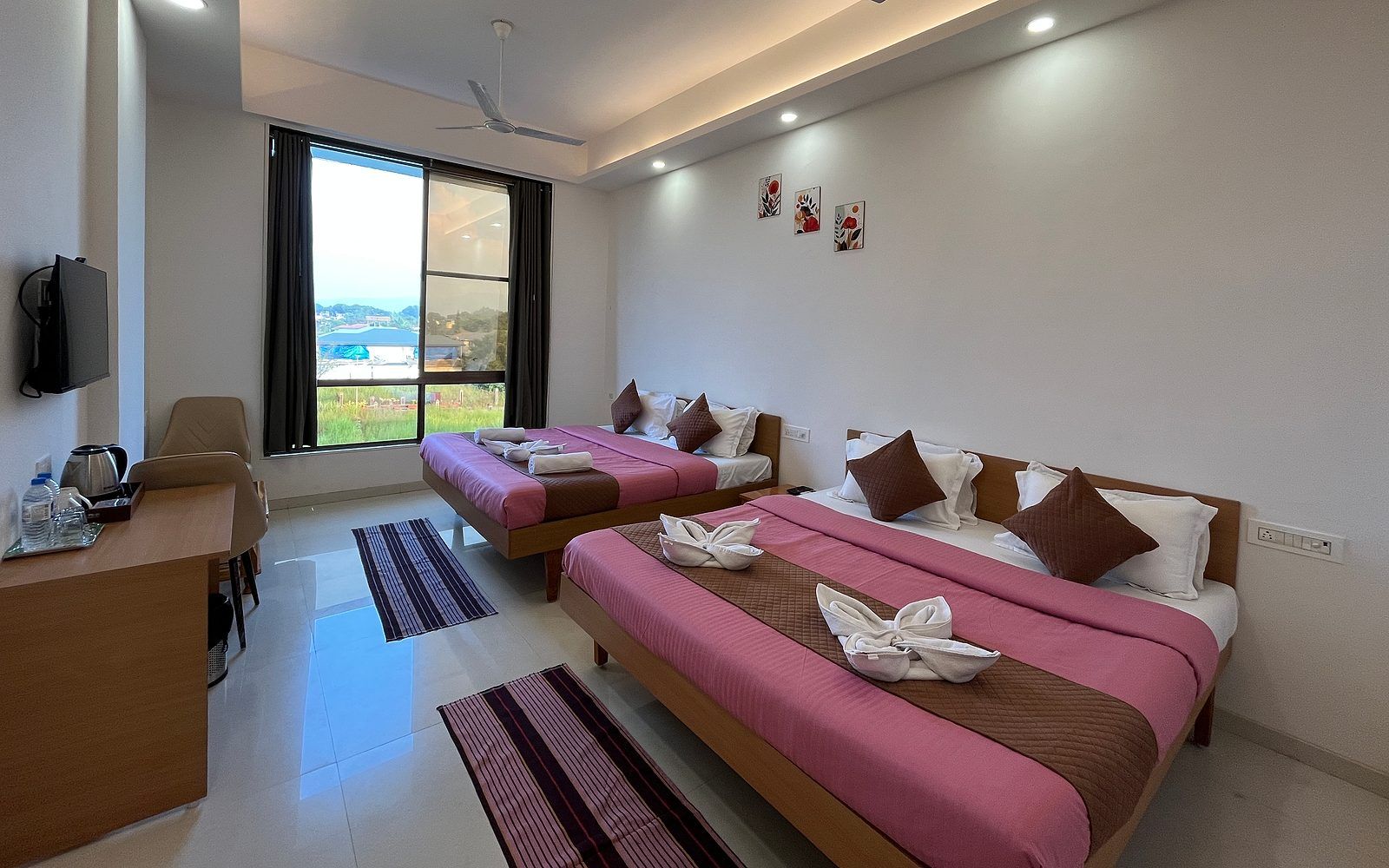 Quarto de hotel com duas camas, uma escrivaninha, televisão de tela plana e uma janela grande com vista.
