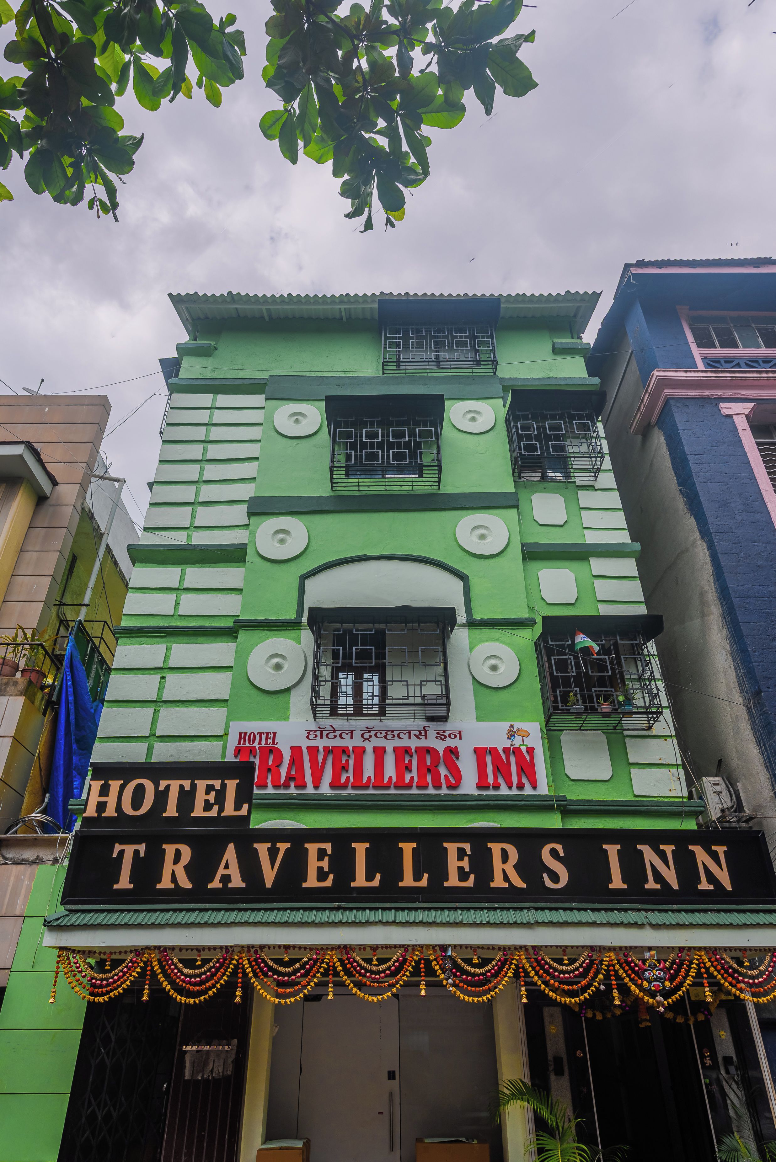 Exterior do hotel Travellers Inn, com fachada verde, placa de identificação e janela com varanda.