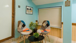 A room with two chairs, a small table, a potted plant, a framed picture on the wall, and a sign with a message.