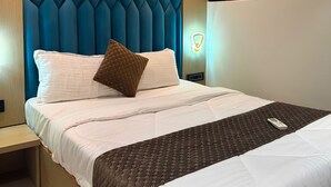 A hotel room with a large bed, a headboard with a geometric pattern, a bedside table, and a wall-mounted light.