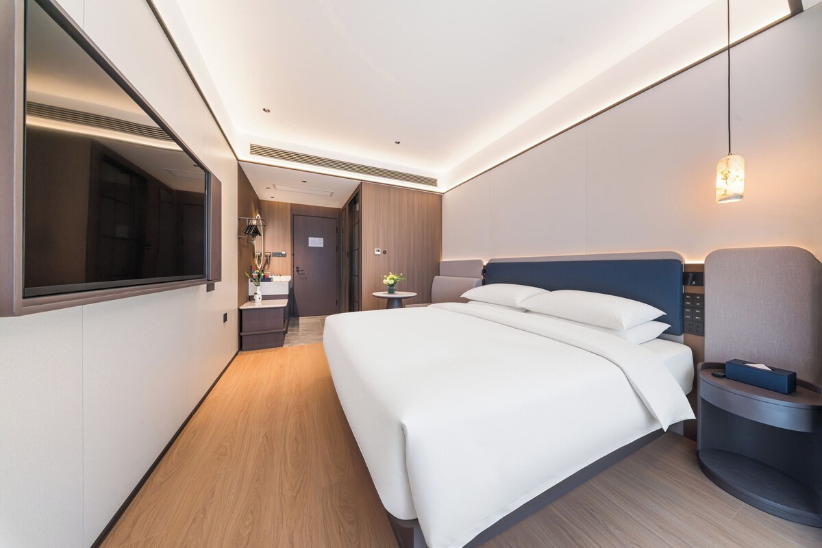 Quarto de hotel moderno com cama grande, mesas de cabeceira, escrivaninha e espelho.