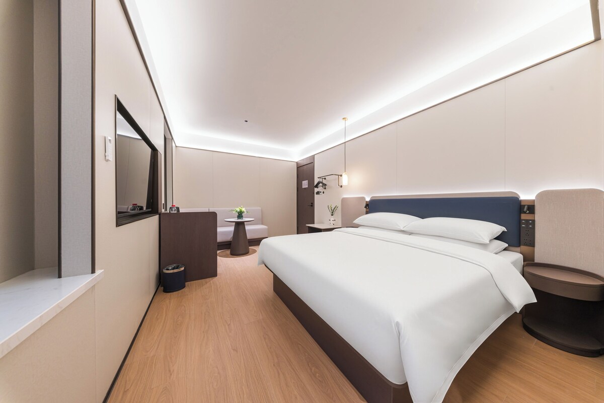 Quarto de hotel moderno com uma cama grande, mesas de cabeceira, escrivaninha e um espelho.