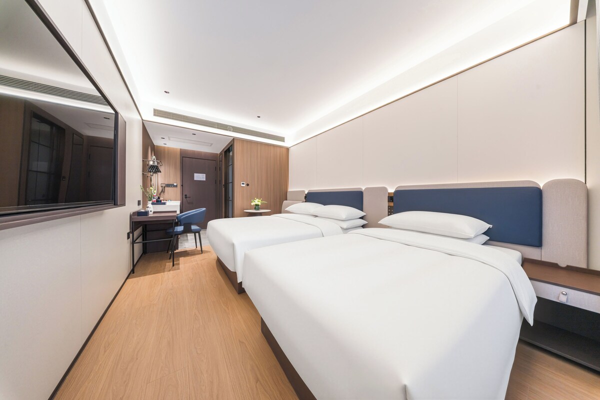 Quarto de hotel com duas camas, uma escrivaninha e um espelho.