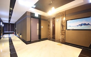 Corredor moderno de hotel com piso lustroso, uma televisão grande fixada na parede e uma porta com painel de vidro.