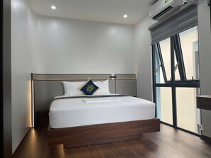 Quarto de hotel moderno com uma cama grande, cabeceira, janela com persianas e unidade de ar condicionado.