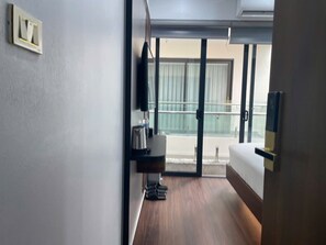 Quarto de hotel com uma cama, uma secretária pequena com uma cadeira, uma TV na parede e uma varanda com vista.