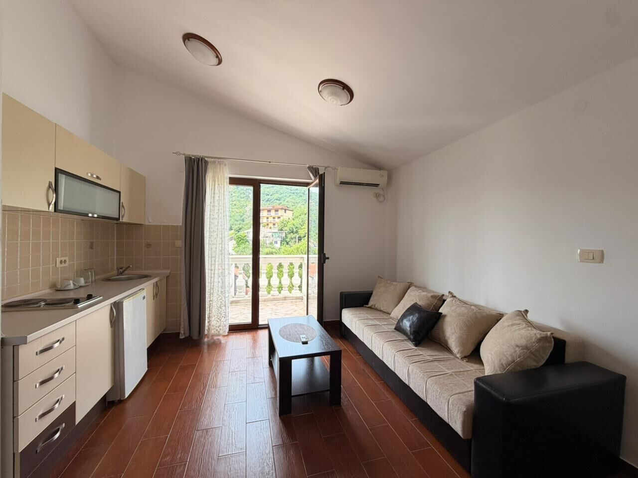 Um espaço de estar compacto com cozinha compacta, sofá, mesa de centro e varanda com vista.