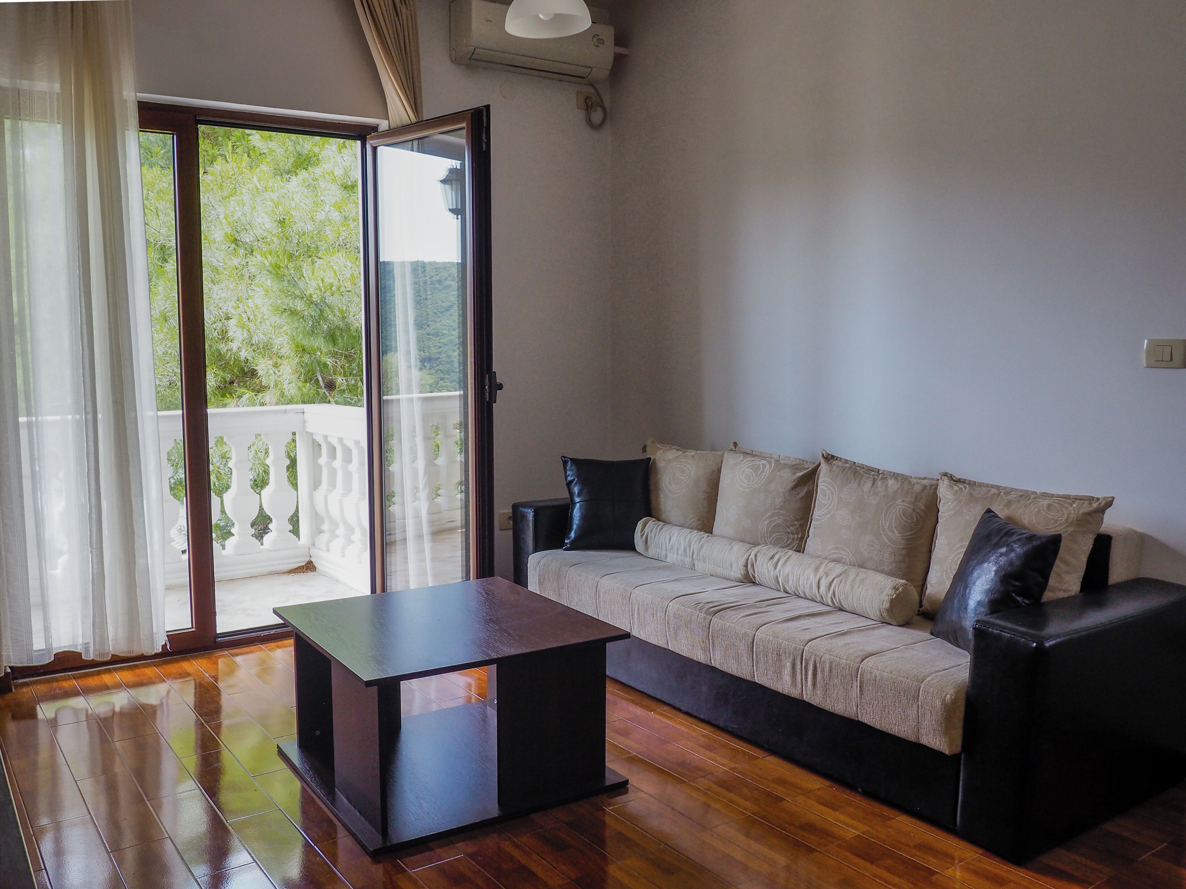 Uma sala de estar com sofá, mesa de centro e porta de vidro corrediça que dá para uma varanda.