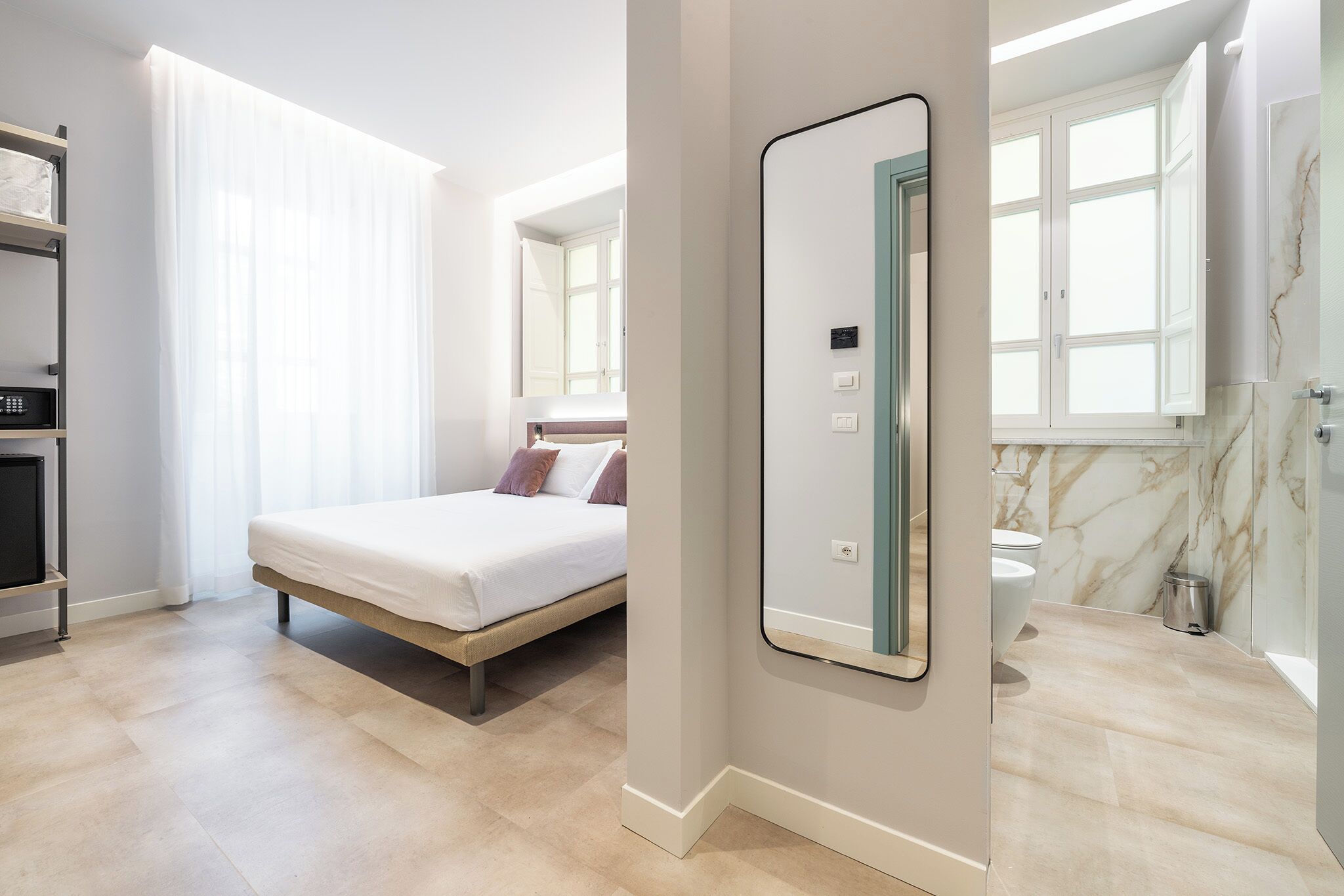 Quarto de hotel moderno com cama, banheiro com lavatório de mármore e um espelho grande.