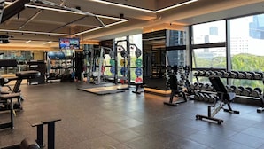 Academia com equipamentos de musculação, esteiras e uma tela de televisão.