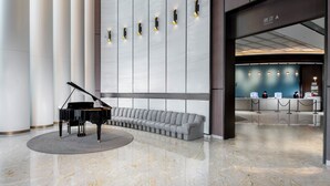 Um saguão de hotel com um piano de cauda, um balcão de recepção e uma área de estar.
