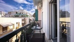 Varanda com mesa e cadeiras, porta de correr e vista para edifícios próximos.