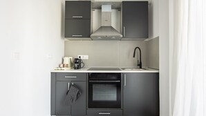 Uma cozinha moderna com armários cinza, forno de aço inoxidável, torneira preta e bancada branca.