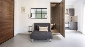Quarto moderno com um sofá-cama cinza, um guarda-roupa de madeira, um quadro emoldurado e vista para a cozinha.