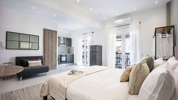 Quarto de hotel moderno com uma cama grande, sofá, mesa de jantar e cozinha compacta.