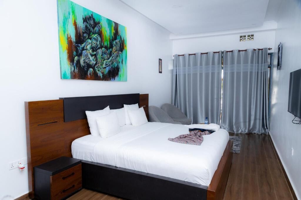 Um quarto moderno com cama de madeira, roupa de cama branca, uma grande pintura abstrata, cortinas cinzas e uma televisão.
