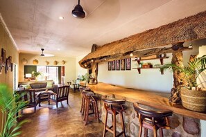 Uma área de bar com design rústico, incluindo um telhado de palha e banquetas de madeira.