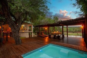 Uma área de piscina com deck de madeira, espreguiçadeiras, pérgola e vista para a paisagem.