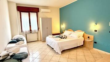 Quarto com cama, mesa de cabeceira, guarda-roupa, radiador e janela com cortinas.