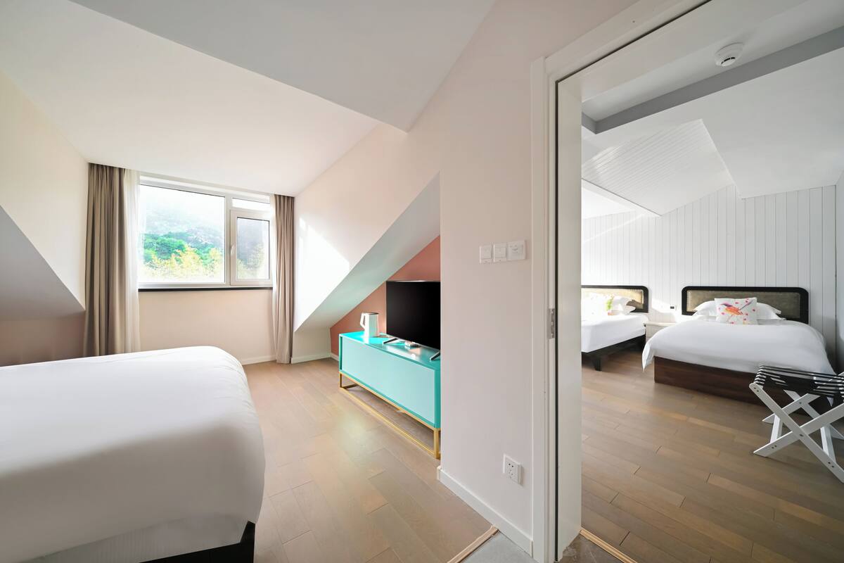 Quarto de hotel com duas camas, cômoda azul-turquesa e uma janela grande com cortinas.