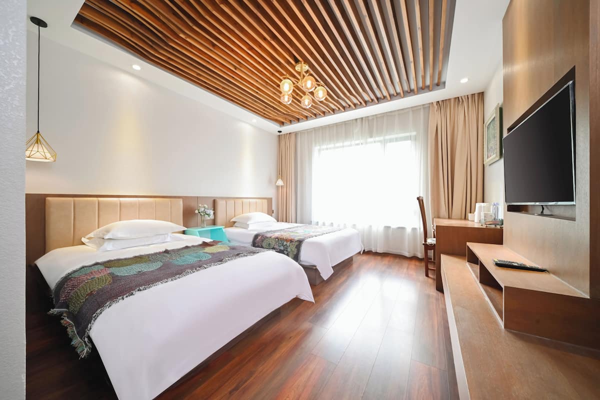 Quarto de hotel com duas camas, televisão, escrivaninha e teto de madeira.