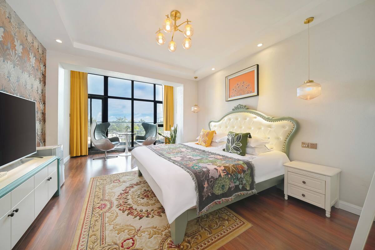 Quarto com uma cama grande, televisão, mesa de cabeceira, abajur e vista para o exterior.